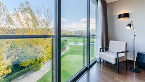 Quarto moderno com grandes janelas, um sofá, um abajur e vista para uma paisagem verde.