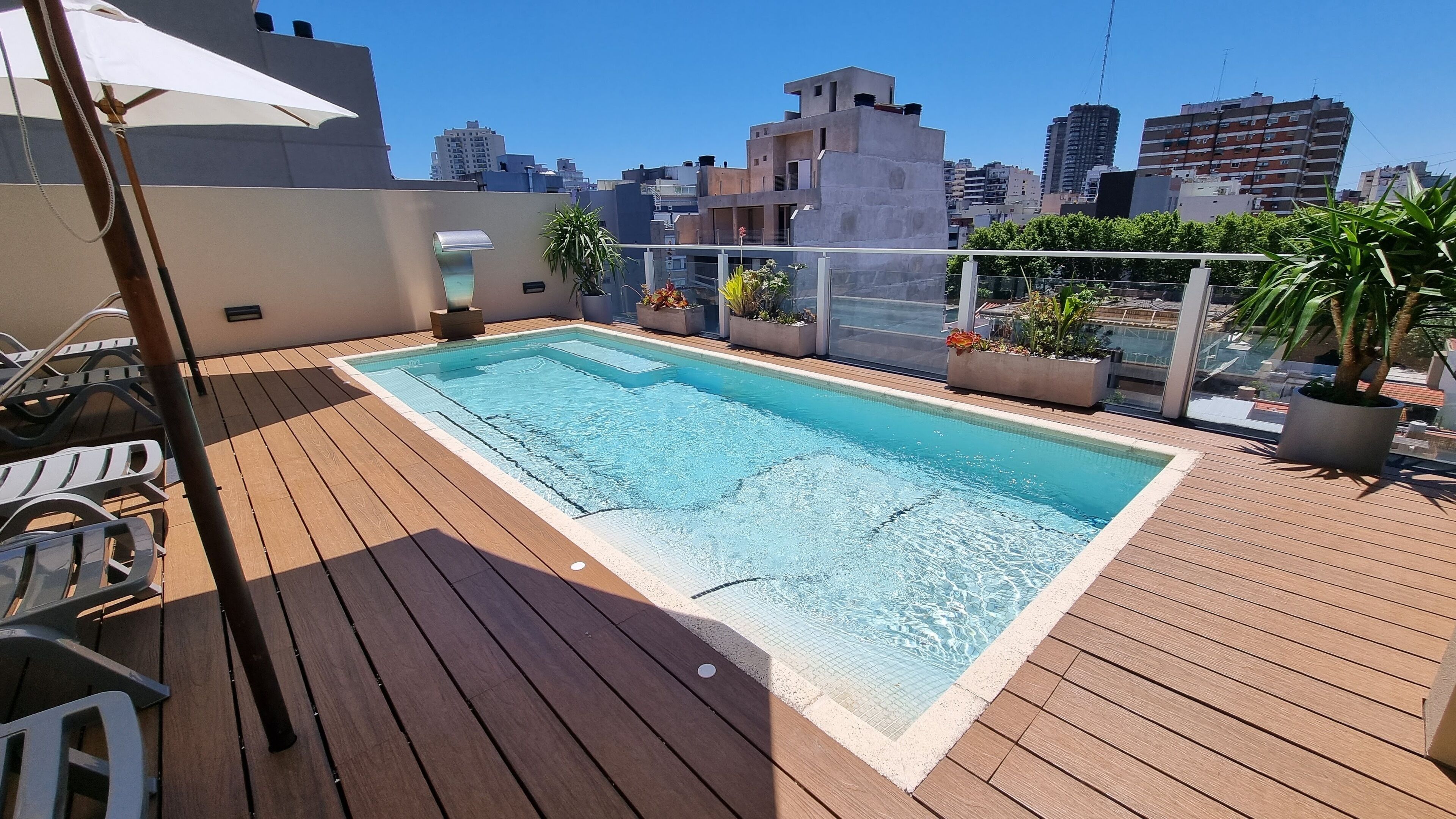 Piscina no terraço com deck de madeira, plantas em vasos e vista panorâmica da cidade.