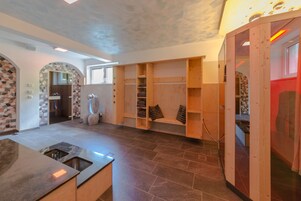Cozinha ampla com bancada de granito e pia embutida. Há prateleiras de madeira e parede de pedra com design em mosaico.