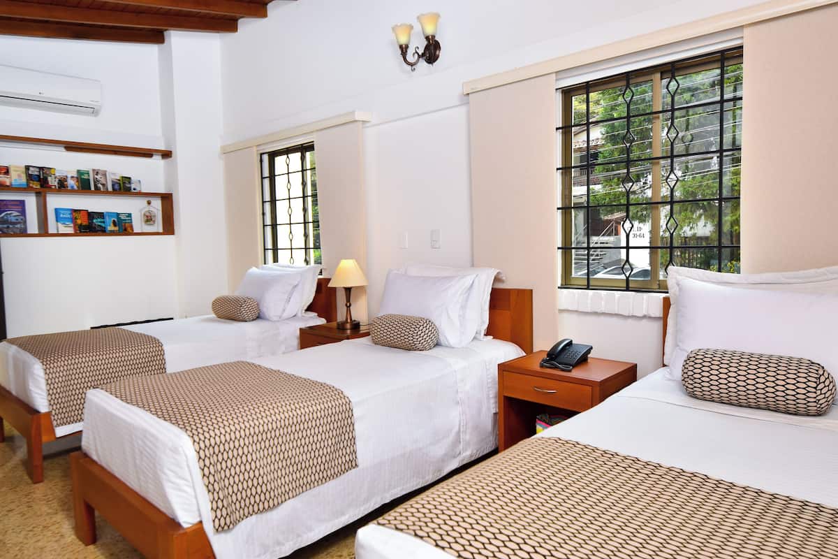 Quarto de hotel com duas camas de solteiro, uma janela grande com vista, mesa de cabeceira com abajur e prateleira com livros.