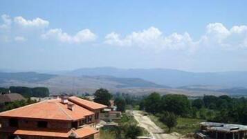 Vista de uma área residencial com casas, estrada de terra e montanhas ao longe, sob um céu claro.