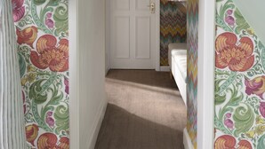 Um corredor estreito com papel de parede floral, uma porta branca e um papel de parede estampado.