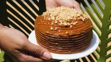 Uma pessoa segurando um bolo em camadas com cobertura de caramelo e nozes sobre um prato branco.