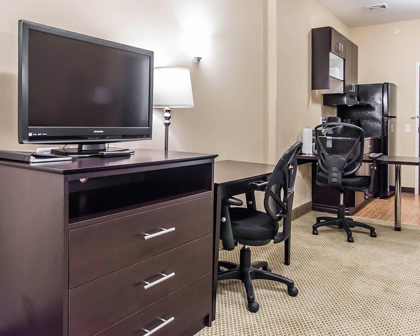 Quarto de hotel com escrivaninha, televisão, cadeira e armário.
