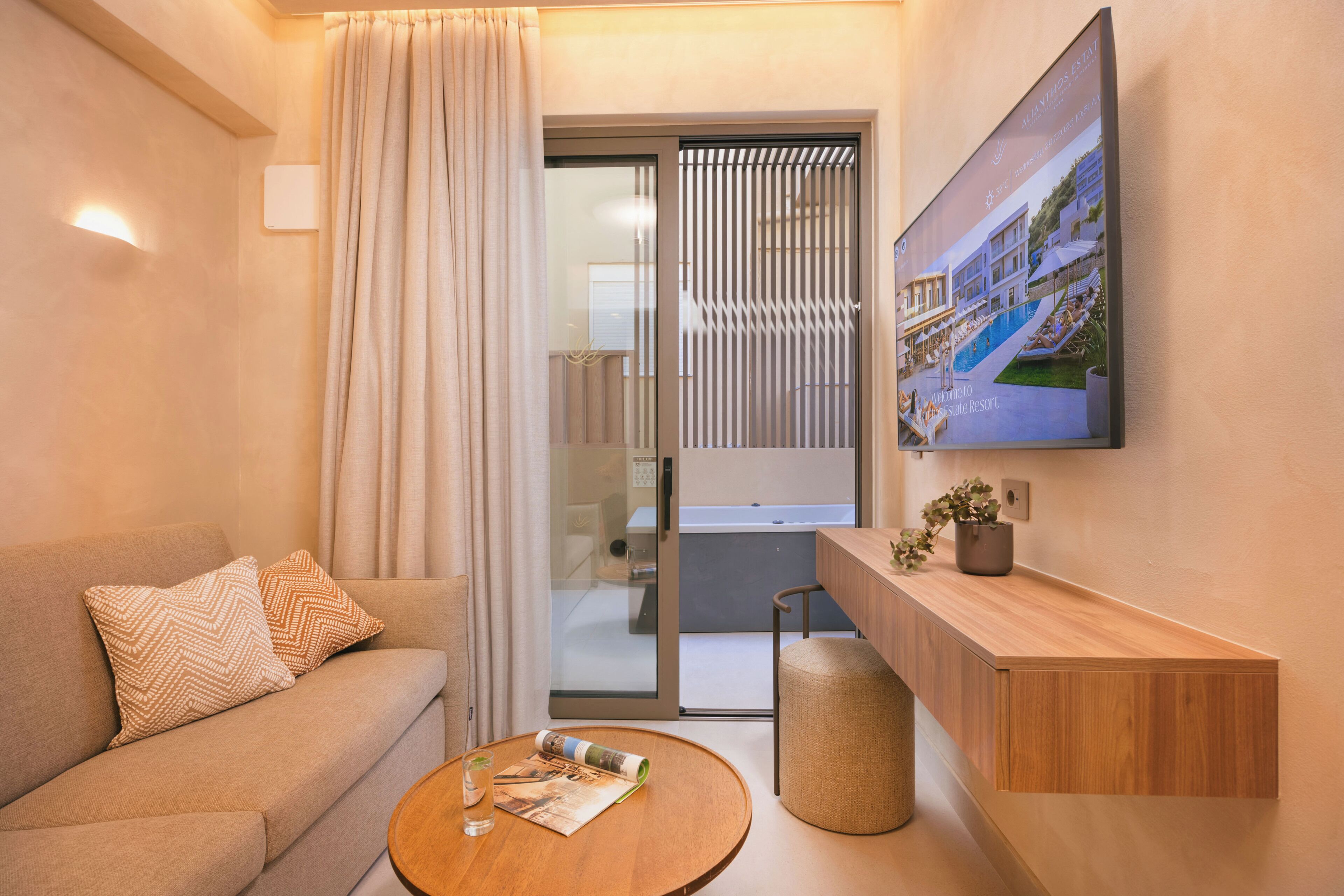 Uma sala de estar moderna com sofá, mesa de centro, revista, planta em vaso e televisão na parede exibindo um resort.
