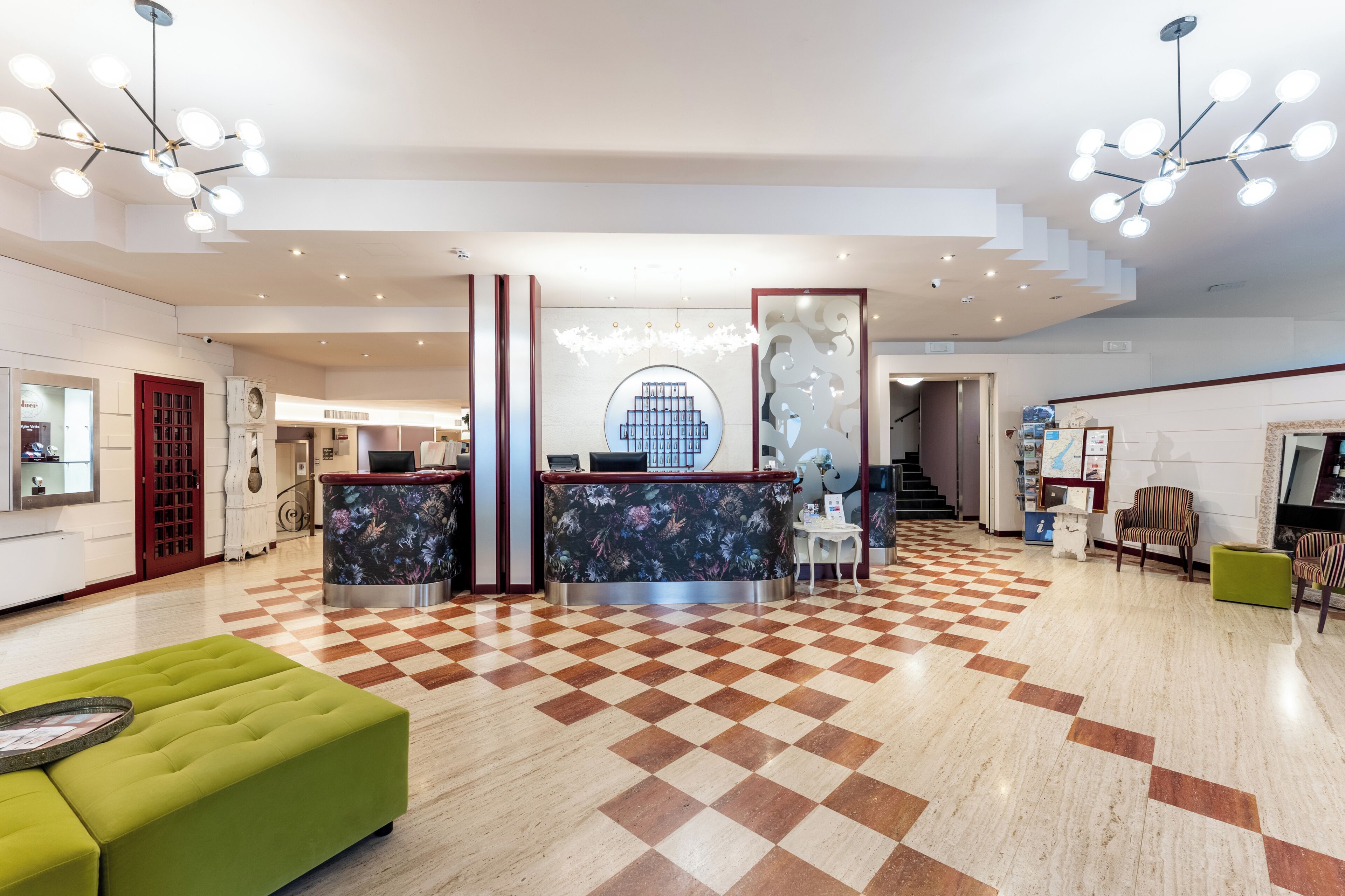 Um hall de hotel com piso xadrez, um balcão de recepção, um sofá verde e uma escadaria.