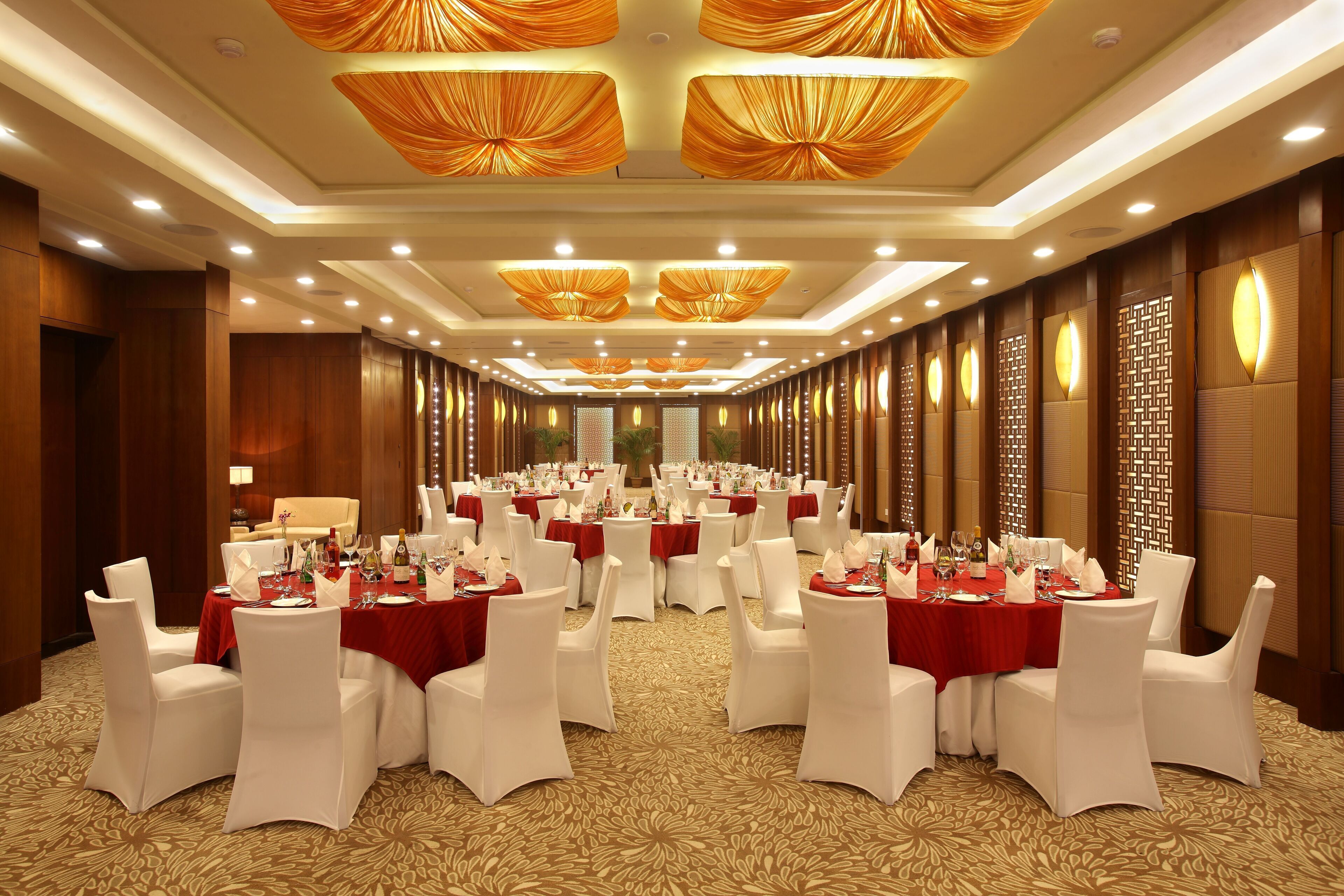 Uma sala de banquetes com mesas redondas, cadeiras brancas e toalhas vermelhas.