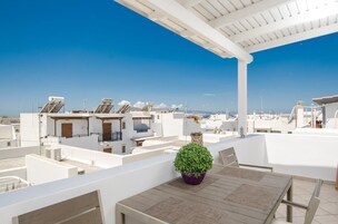 Terraço no telhado com pérgola, uma mesa e um vaso de planta.