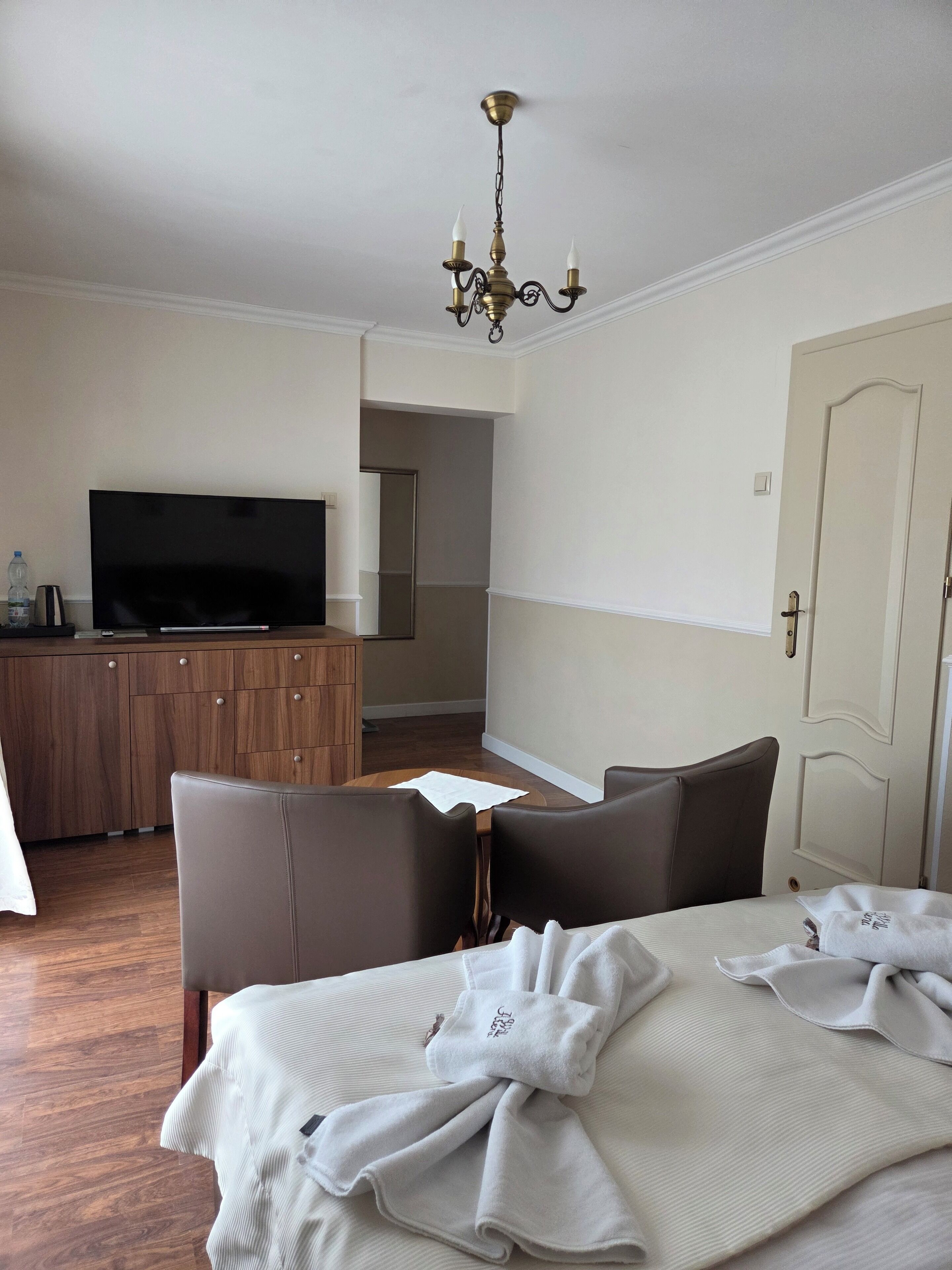 Quarto de hotel com cama, televisão, armário de madeira e lustre.