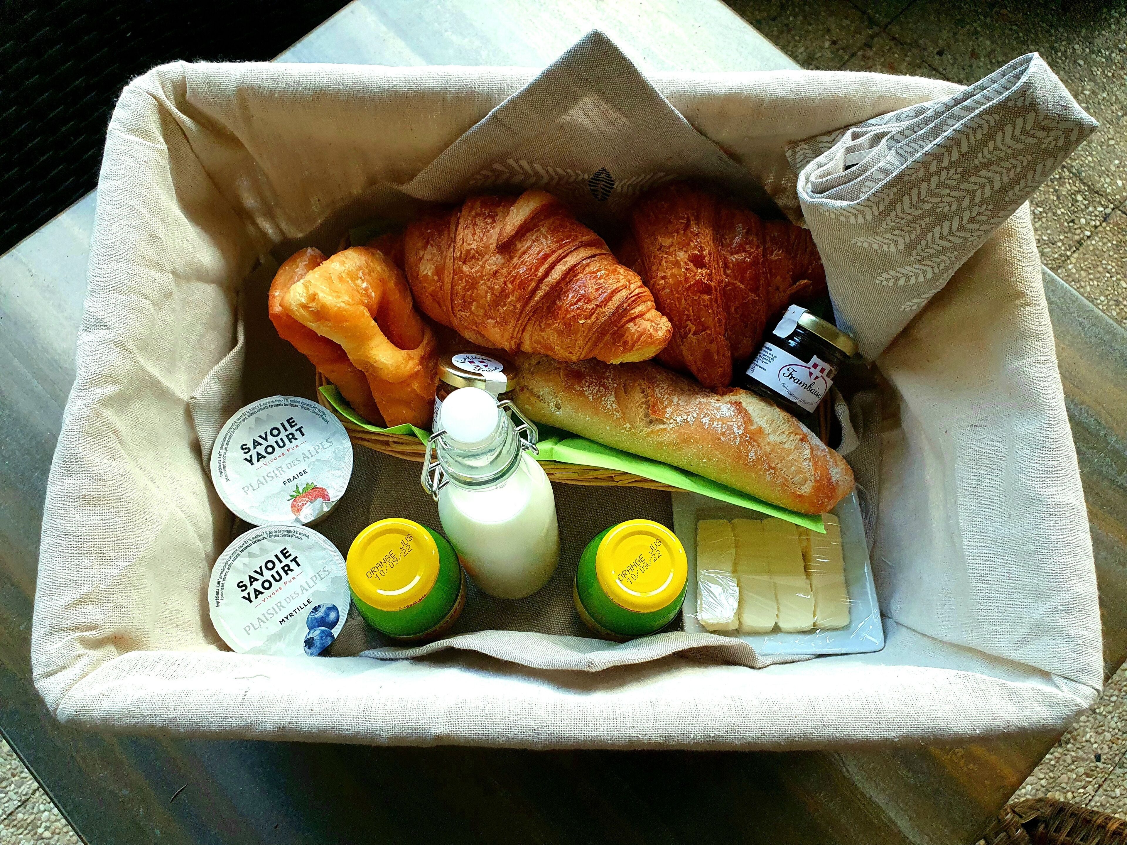 Uma cesta com um croissant, uma baguete, uma garrafa de leite e dois potes de iogurte.