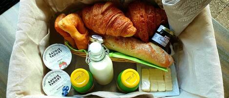 Uma cesta com um croissant, uma baguete, uma garrafa de leite e dois potes de iogurte.