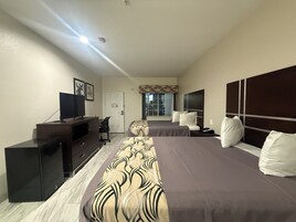 Quarto de hotel com uma cama grande, uma escrivaninha com computador, televisão e janela com vista para edifícios.