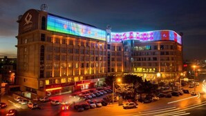 Um hotel com vários andares, sinalização iluminada e estacionamento.