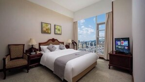 Quarto de hotel com cama grande, uma cadeira, televisão e janela com vista para a cidade.