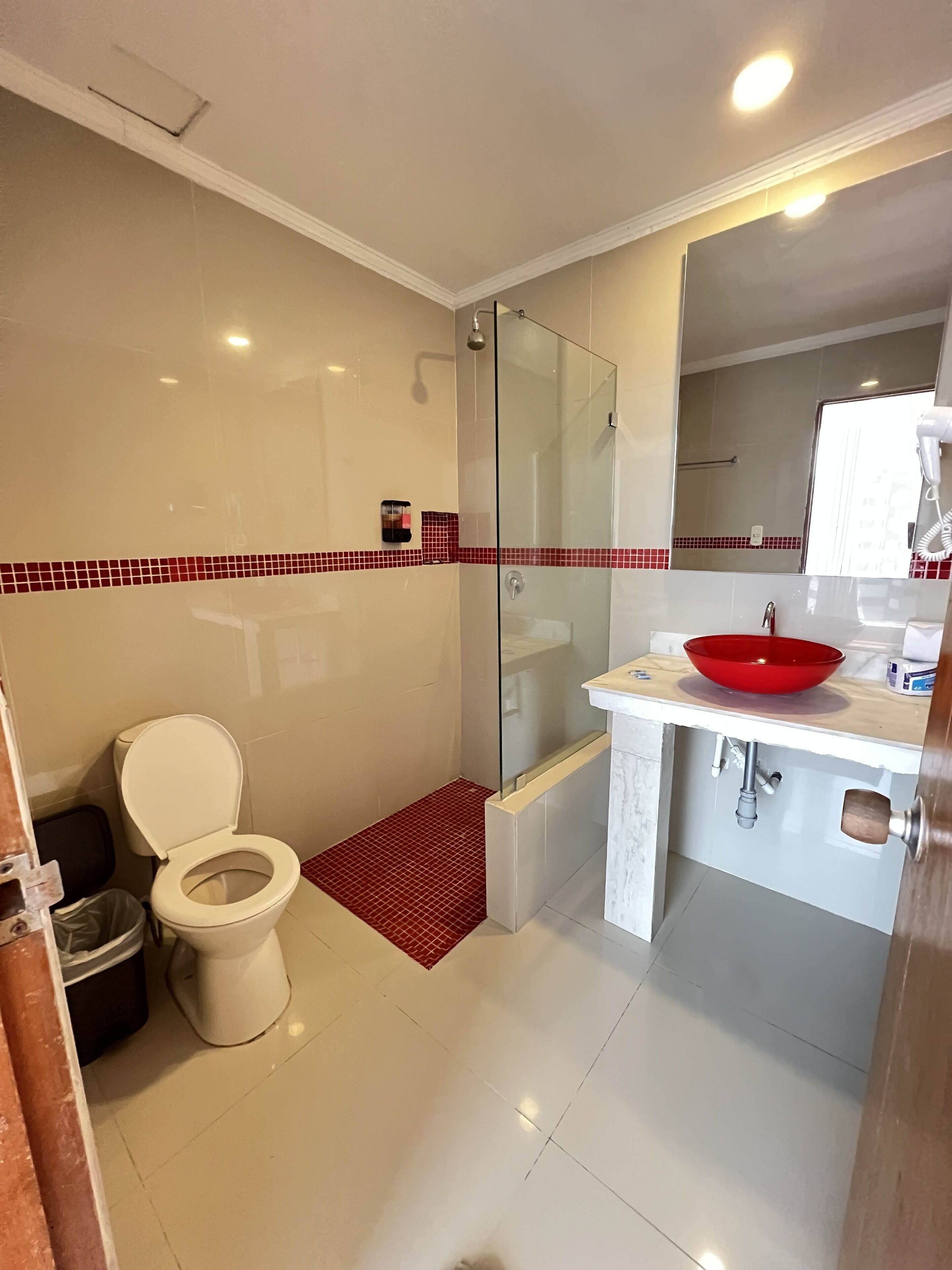 Casa de banho com sanita, cabine de duche em vidro, lavatório com bacia vermelha e espelho.