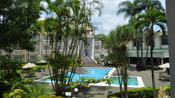 Pátio de hotel com piscina, palmeiras e áreas de estar ao ar livre.