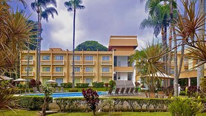 Um hotel com vários andares, piscina e palmeiras.