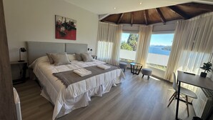 Quarto com uma cama grande, uma escrivaninha e vista para o mar.