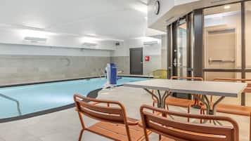 Uma área de piscina com cadeira do salva-vidas, escada para piscina e mesa com cadeiras.