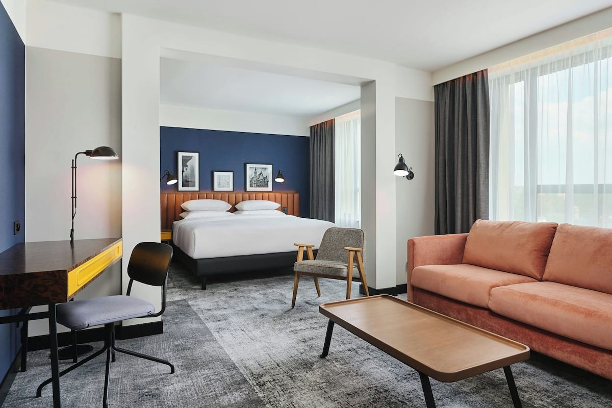Quarto de hotel com cama, sofá, escrivaninha, cadeira e mesa de centro.