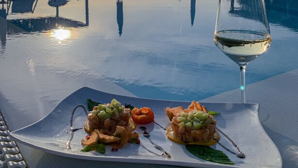 Mesa à beira da piscina com um copo de vinho branco e dois petiscos.