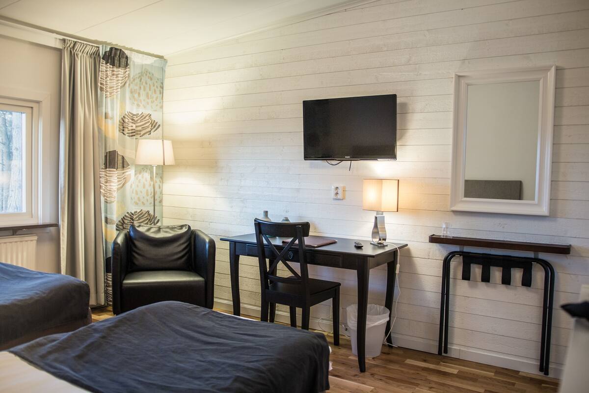 Quarto de hotel com duas camas, uma mesa de trabalho com cadeira, televisão e espelho.