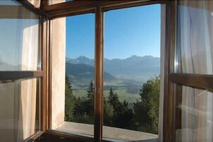 Quarto com uma grande janela que oferece vista para uma paisagem montanhosa.