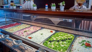 Buffet com diversas opções de comida, incluindo saladas, massas e pratos de arroz.