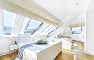 Quarto moderno com uma cama grande, claraboias e vista do céu.