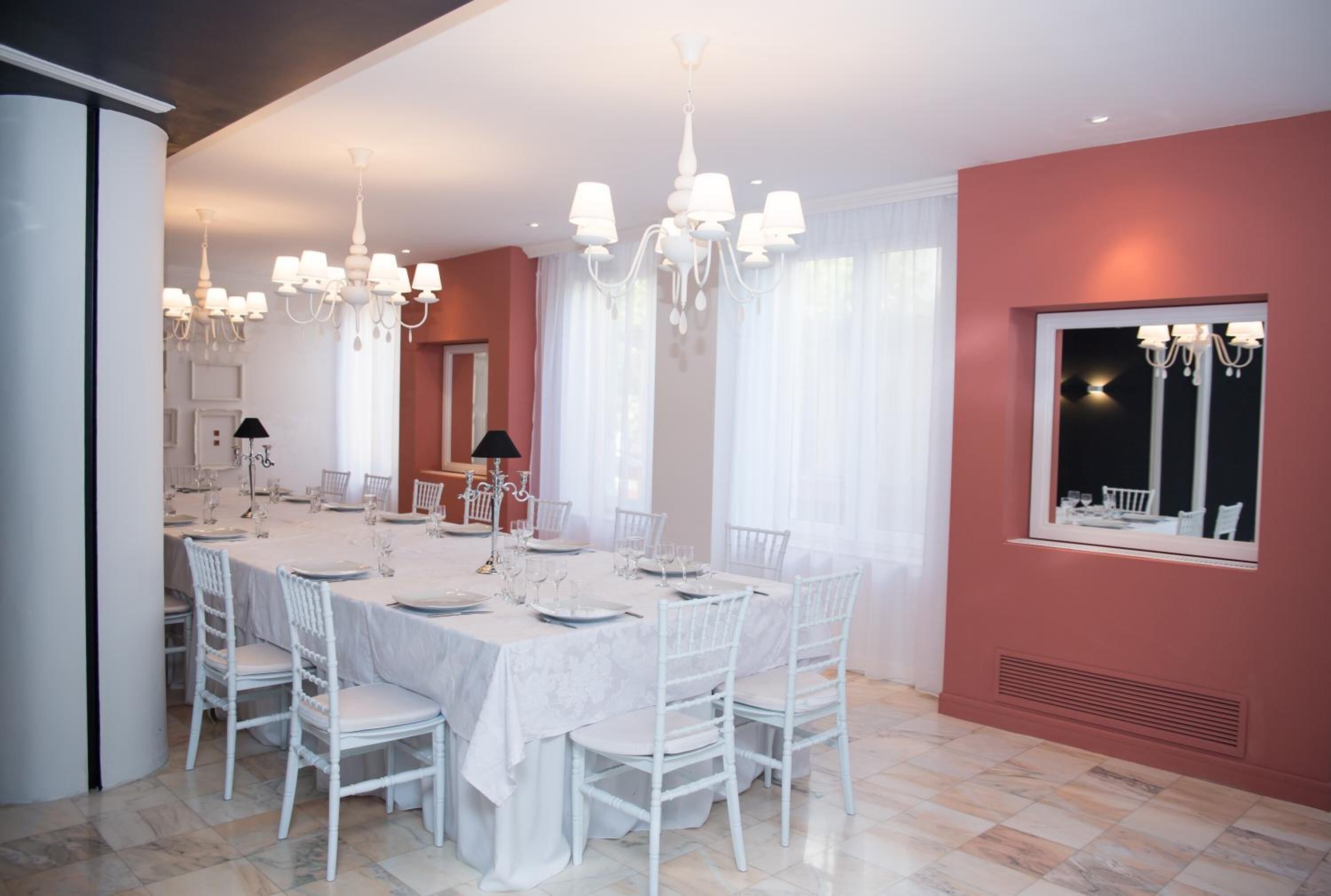 Uma sala de jantar com uma mesa redonda posta para seis pessoas, cadeiras brancas e lustres.
