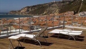 Um deck de madeira com cadeiras de lounge brancas e vista para uma vila costeira e falésias.