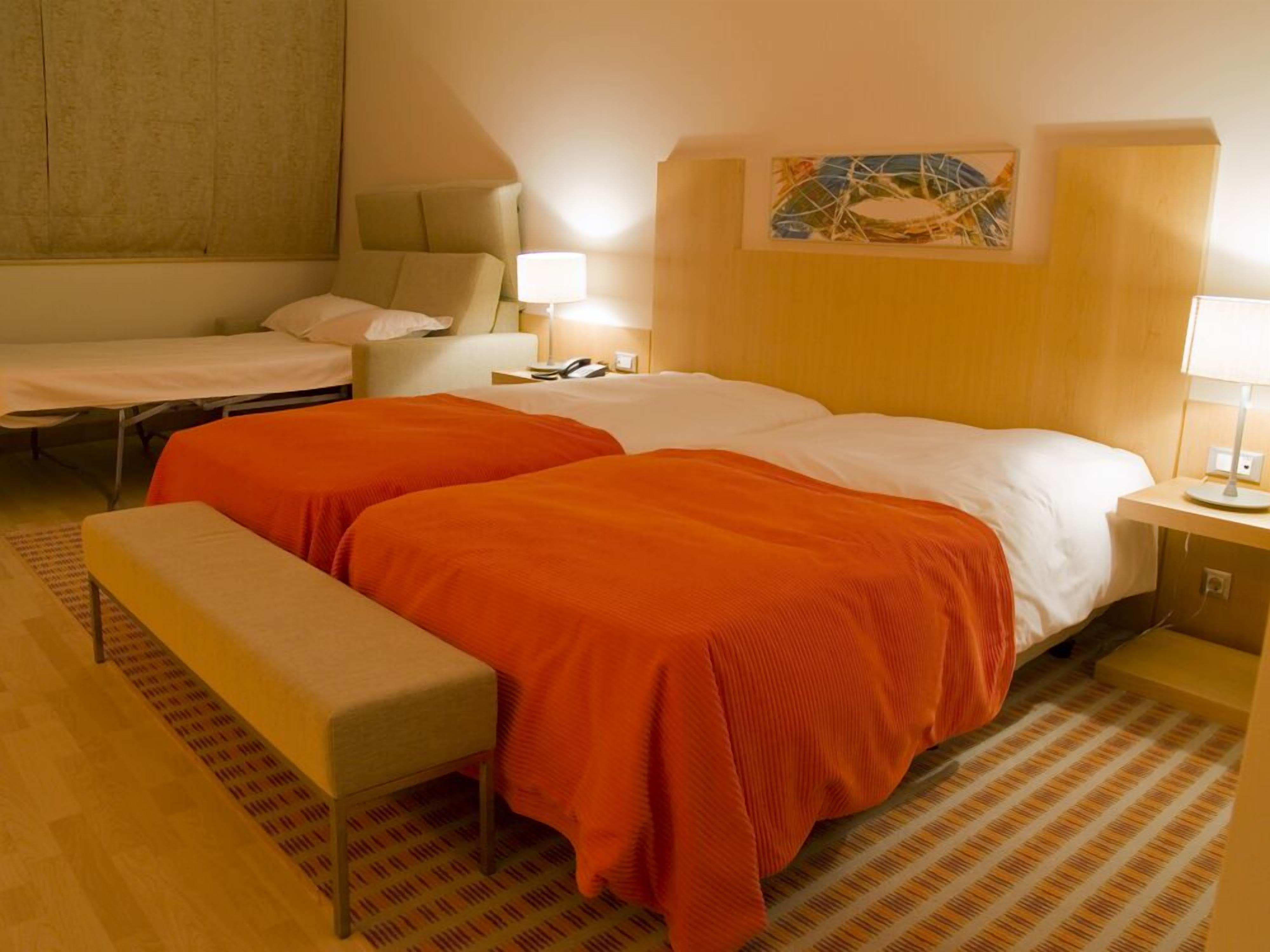 Quarto de hotel com duas camas, um banquinho e um quadro na parede.