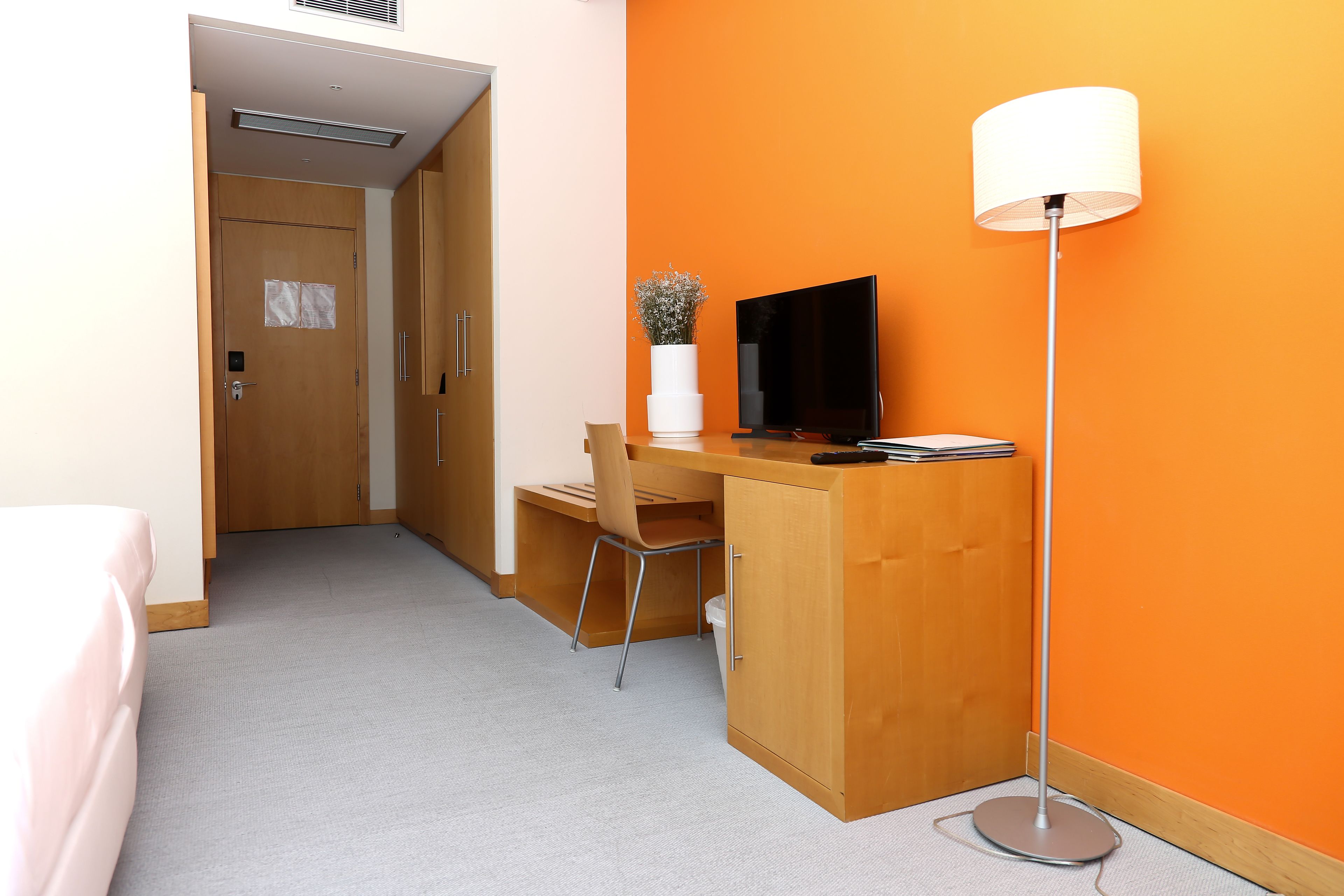 Quarto de hotel com escrivaninha, cadeira, televisão, abajur e um pequeno vaso de planta.