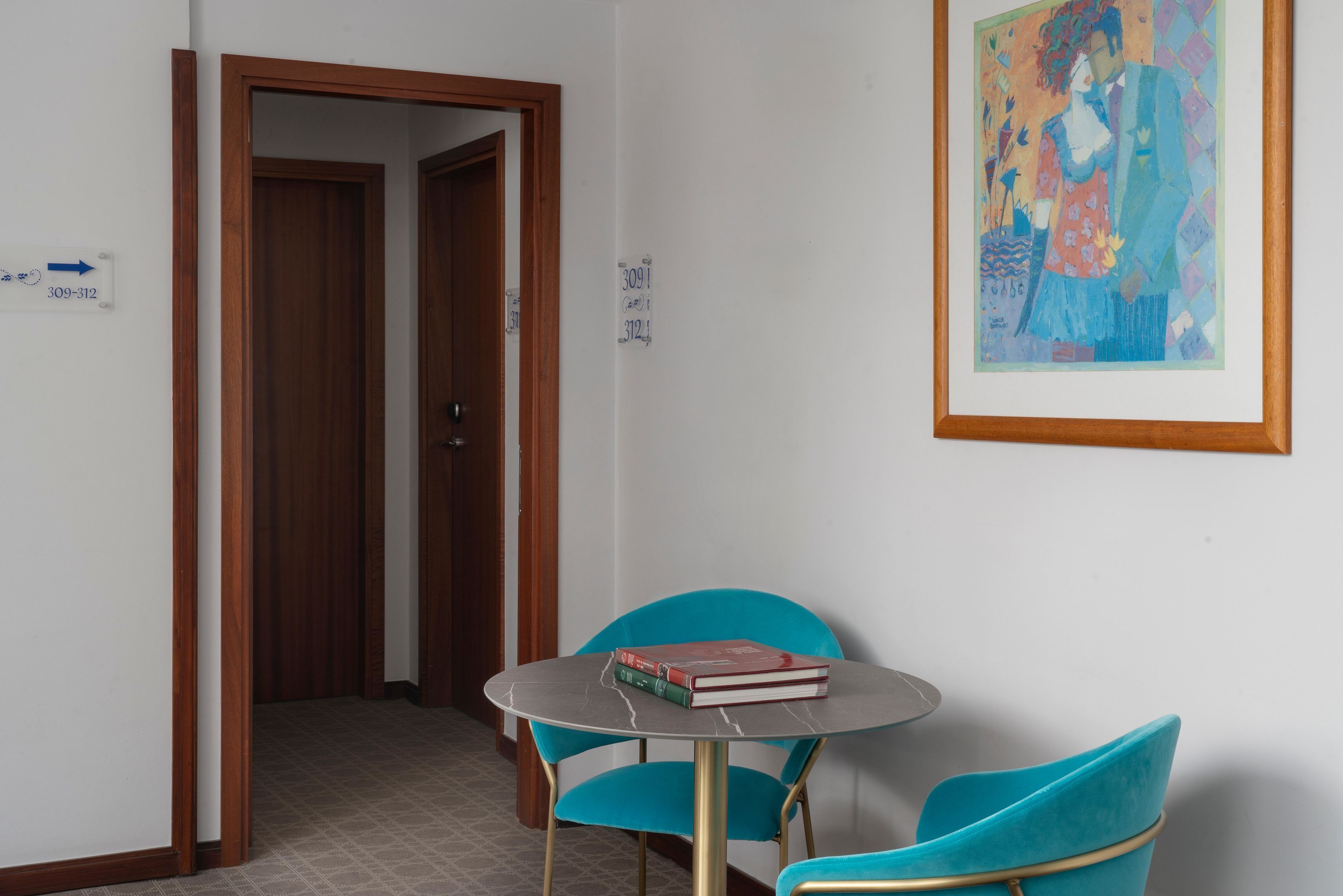 Um quarto com uma pequena mesa redonda, duas cadeiras turquesa e um quadro pendurado na parede.
