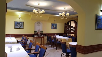 Um restaurante com várias mesas e cadeiras, lustres e obras de arte nas paredes.