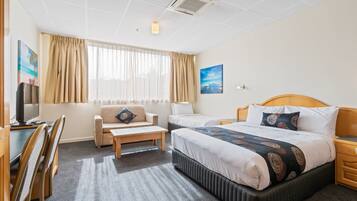 Quarto de hotel com cama, sofá, escrivaninha com cadeira, televisão e janela com cortinas.