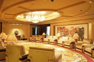 Um saguão de hotel com área de estar circular, um candelabro e uma pintura grande na parede.