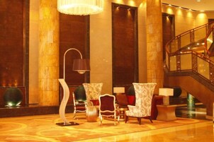 Um hall de entrada com uma escadaria imponente, cadeiras elegantes e uma luminária de chão moderna.