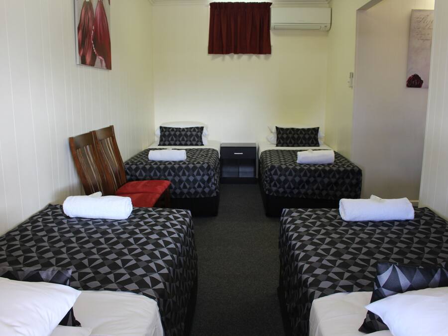 Quarto com duas camas, cada uma com roupa de cama estampada e travesseiros brancos. Há uma cadeira de madeira e uma mesinha entre as camas.