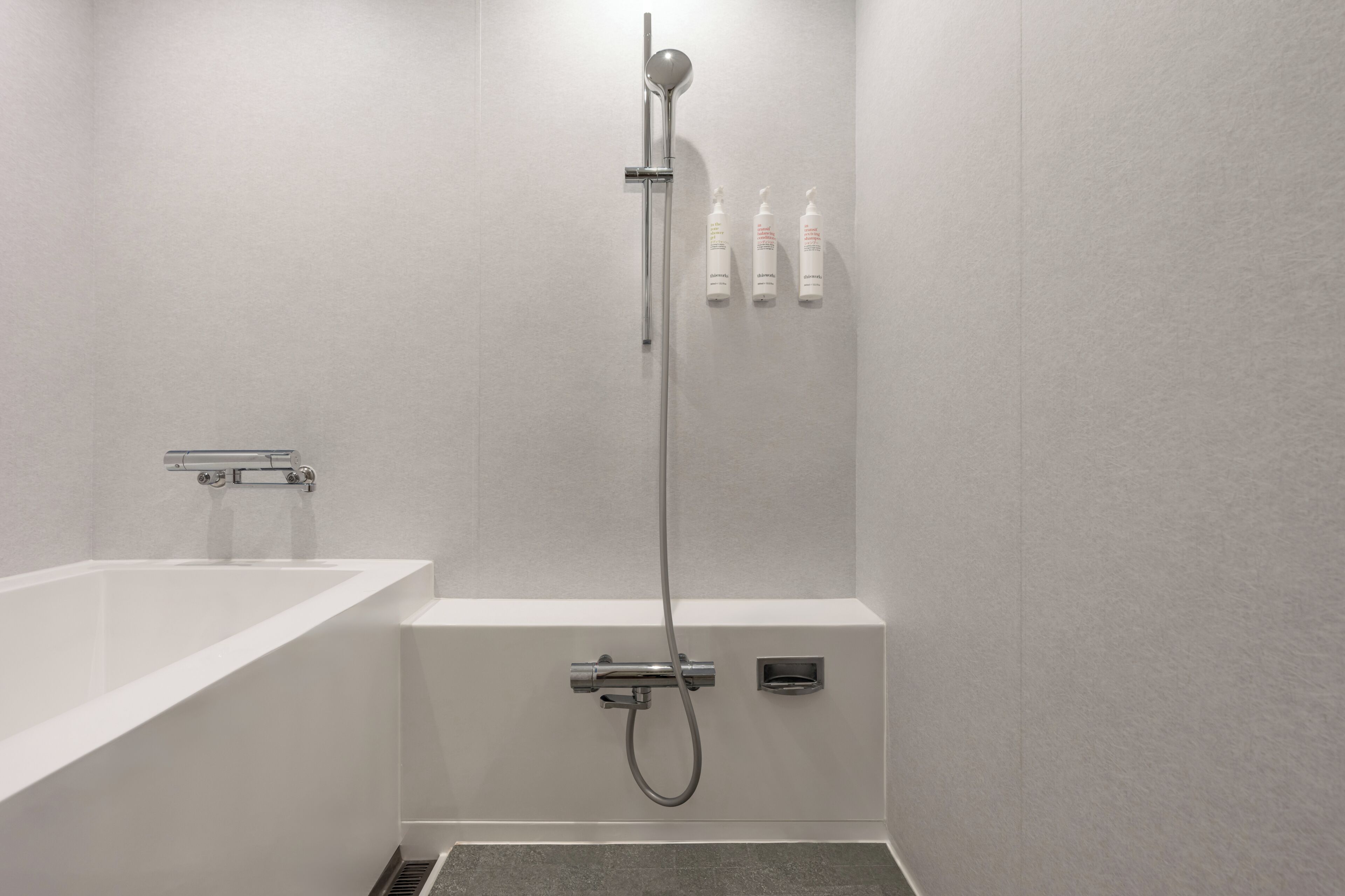 Um banheiro moderno com chuveiro, banheira e três frascos de shampoo.