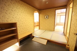 Quarto com piso de tatame, cama de madeira baixa, prateleira com livros e janela com vista.