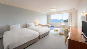 Quarto de hotel com duas camas, uma escrivaninha, televisão e varanda com vista para o mar.
