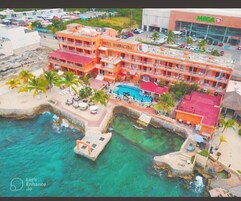 Um hotel com vários andares, área de piscina, palmeiras e vista para a praia.