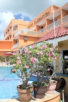 Hotel com área de piscina, plantas em vasos e céu azul claro.