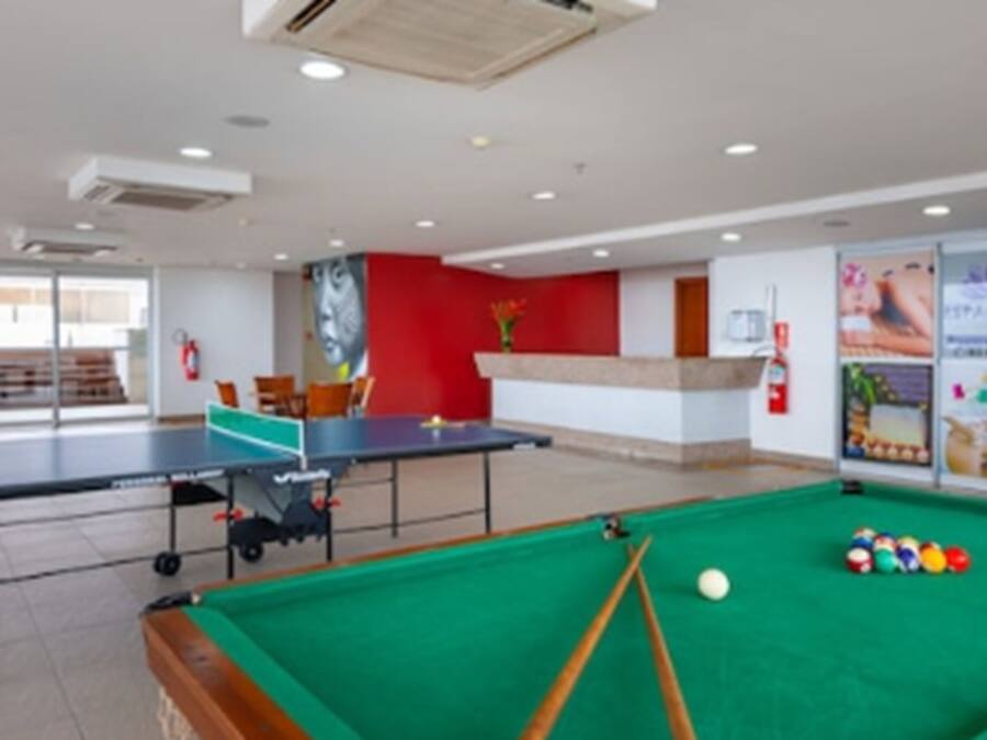 Uma sala de bilhar com duas mesas, uma mesa de sinuca verde e uma mesa vermelha. Há uma receção com uma parede vermelha e um cartaz na parede.