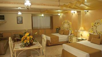 Quarto de hotel com duas camas, uma mesa de jantar com um vaso de flores e uma televisão na parede.