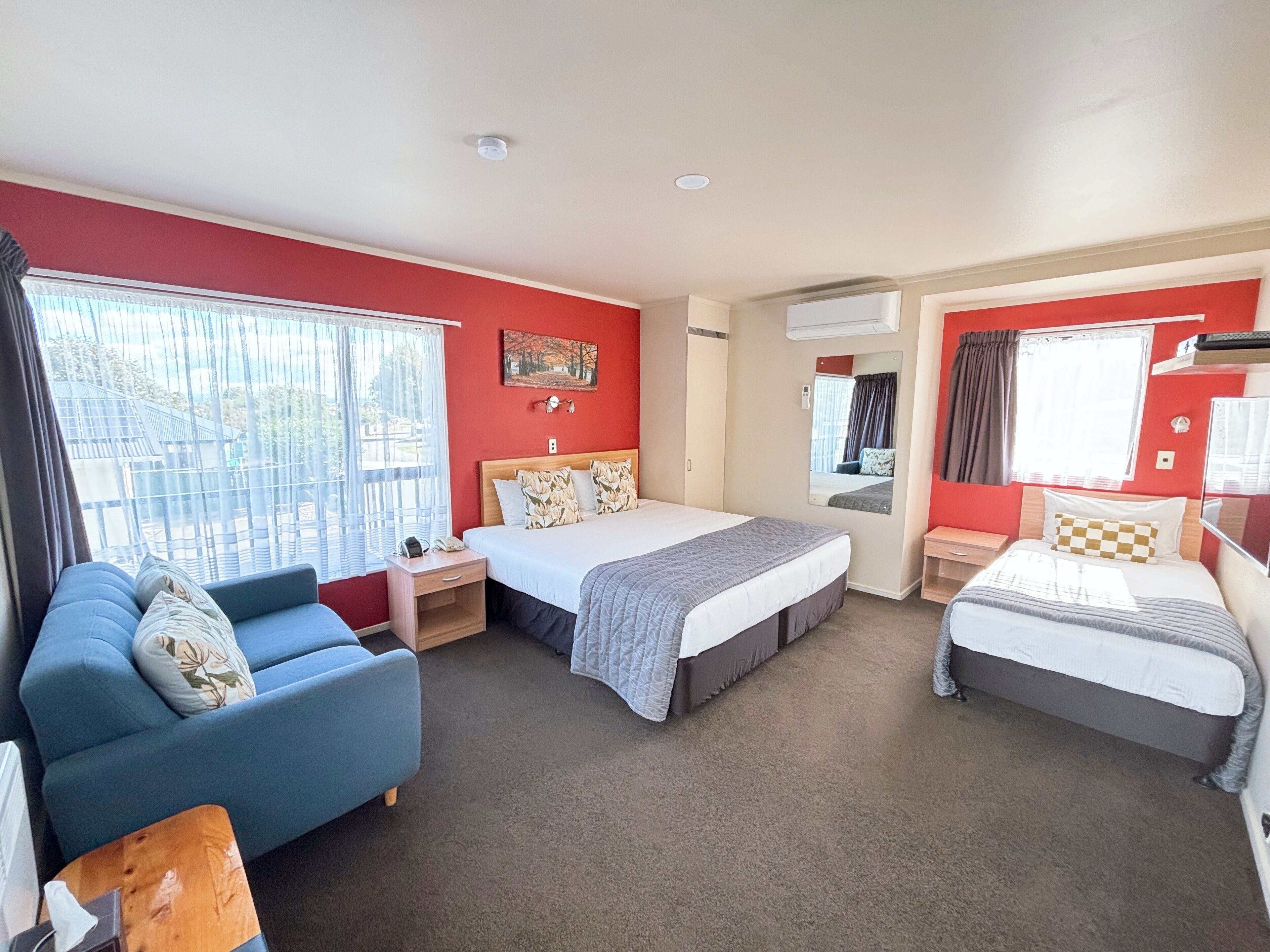 Quarto de hotel com cama grande, sofá, escrivaninha e janela com cortinas.