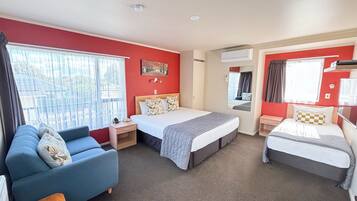 Quarto de hotel com cama grande, sofá, escrivaninha e janela com cortinas.