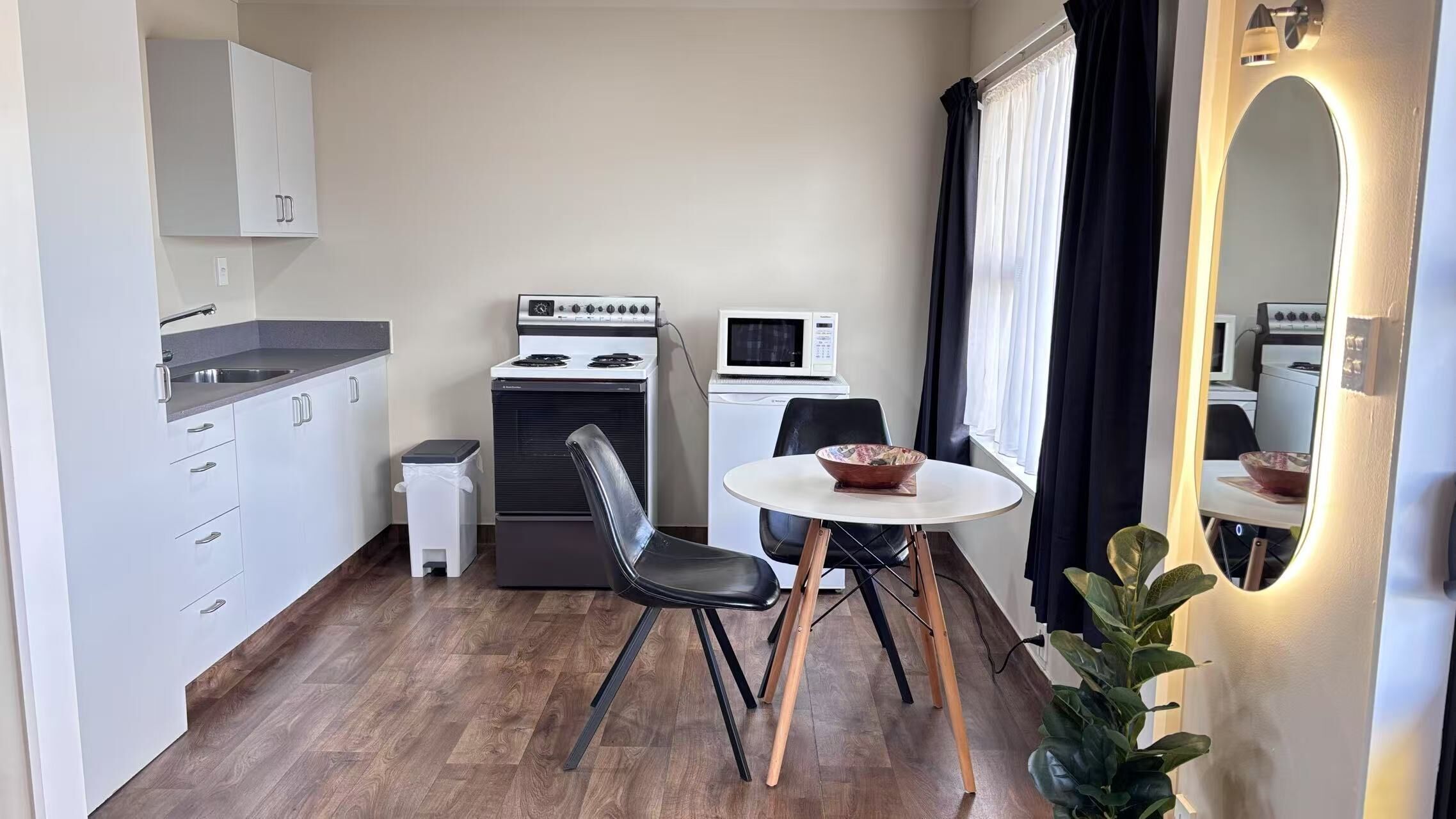 Cozinha compacta com armários brancos, fogão, micro-ondas e área de jantar com mesa e cadeiras.