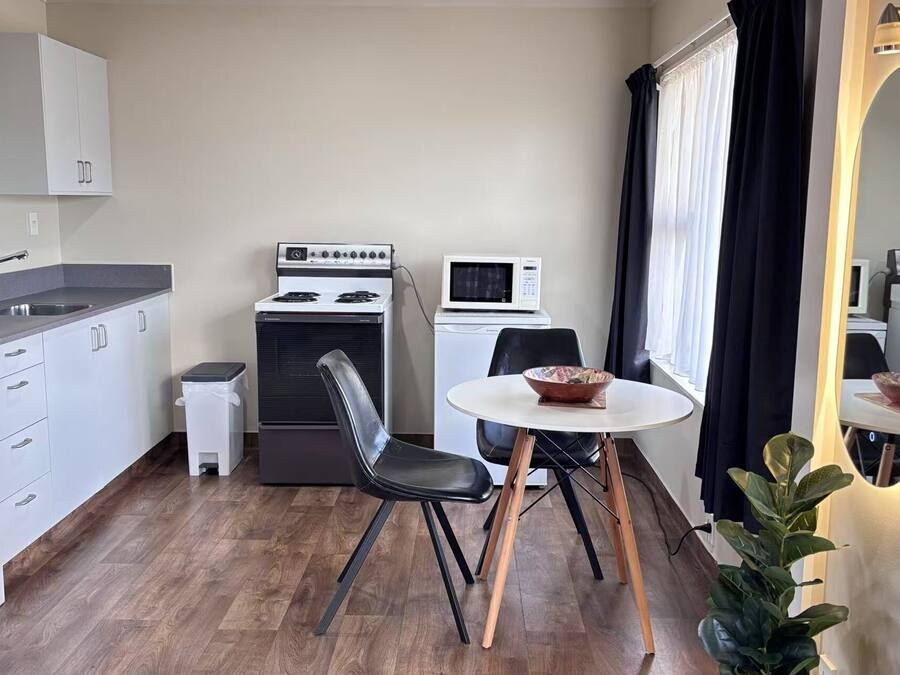 Cozinha compacta com armários brancos, fogão, micro-ondas e área de jantar com mesa e cadeiras.